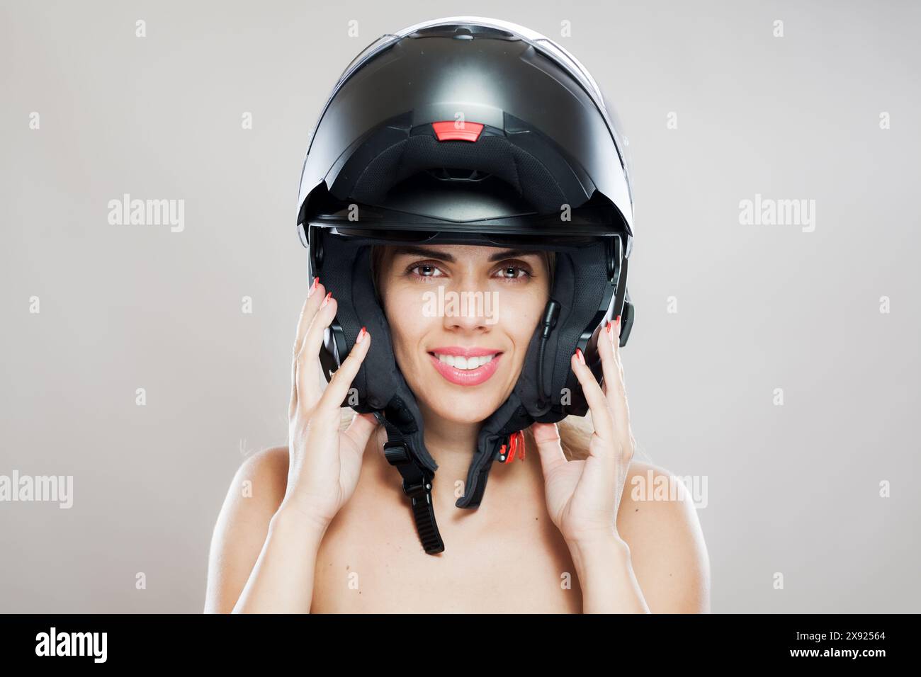 A cheerful young lady fitting a stylish black motorcycle helmet, ready ...