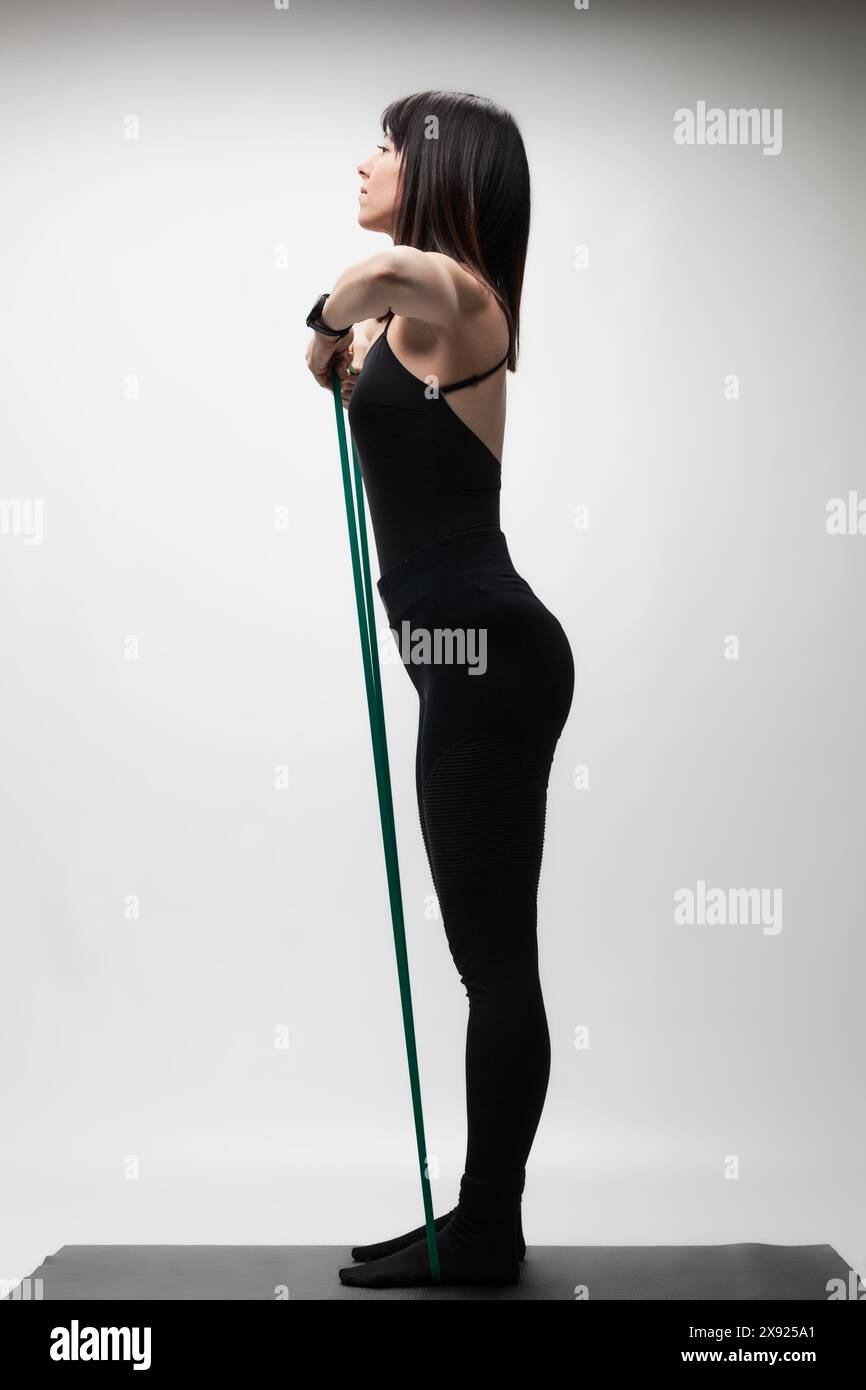 A focused young woman in athletic wear using a resistance band for an ...