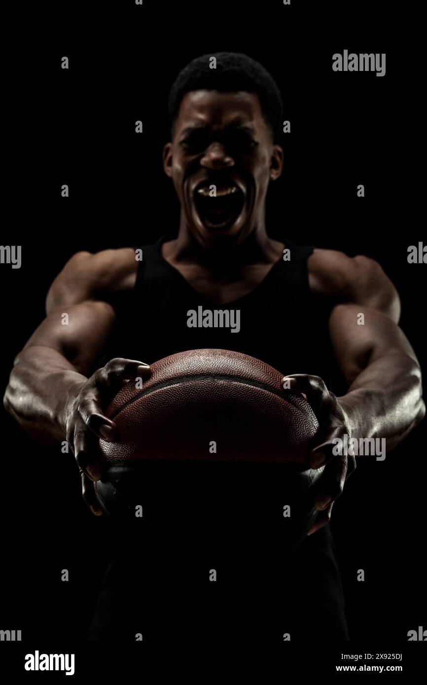 Basketball player holding a ball against black background. Screaming ...