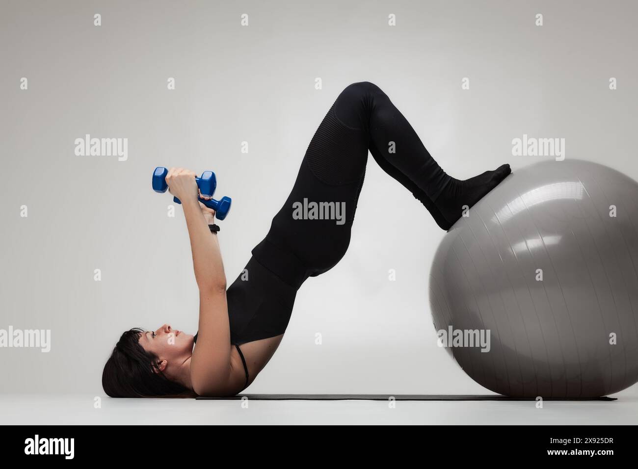 Focused young woman using dumbbells and a stability ball to perform ...