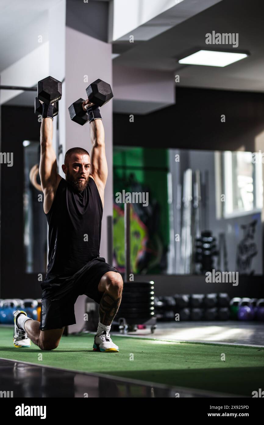 A muscular man performs an overhead dumbbell press in a well-equipped ...