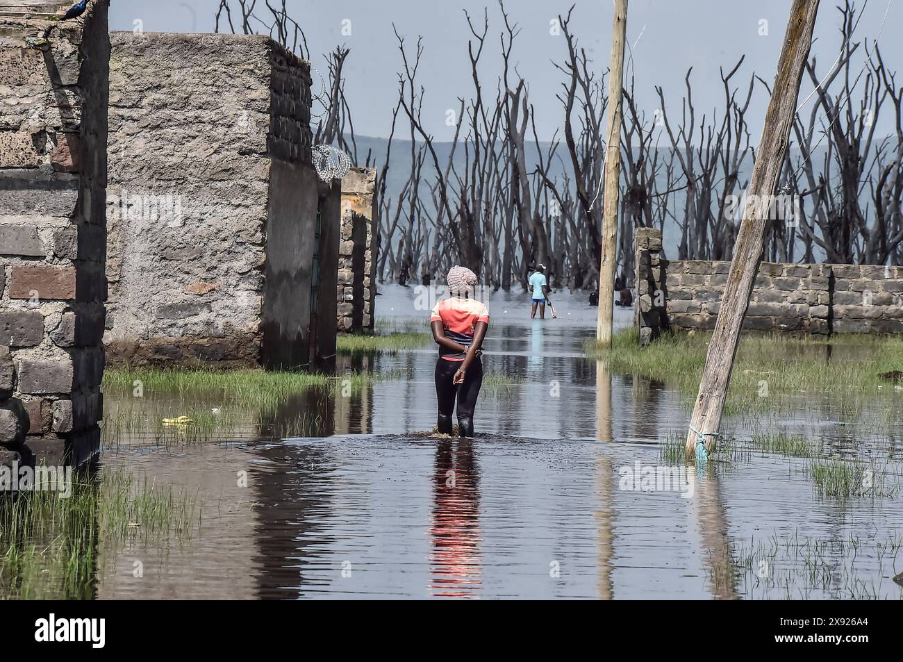A woman wades beside submerged buildings as fishermen cast their nets ...