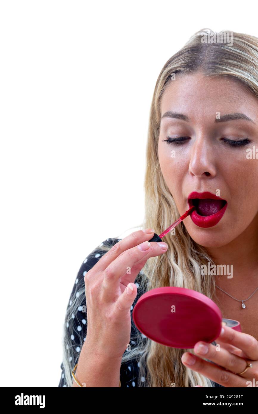 Woman tinting her lips bright red with an applicator Make-up session ...