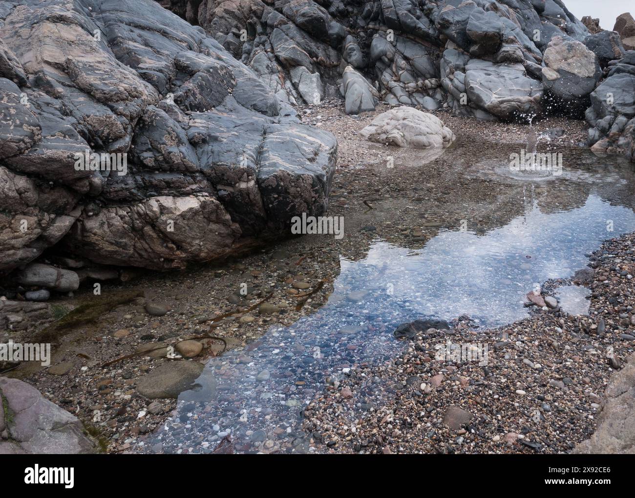 Tidal rock pool at Kennack Sands, Cornwall. Splash of a stone in the ...