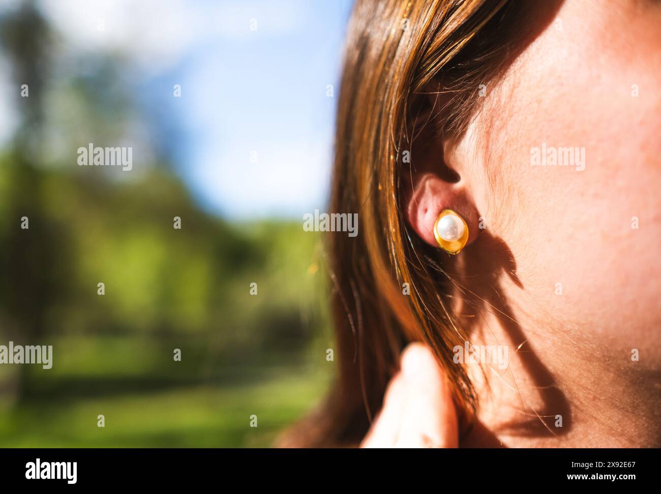 A young woman displays a gold and pearl earring worn on her right ear ...