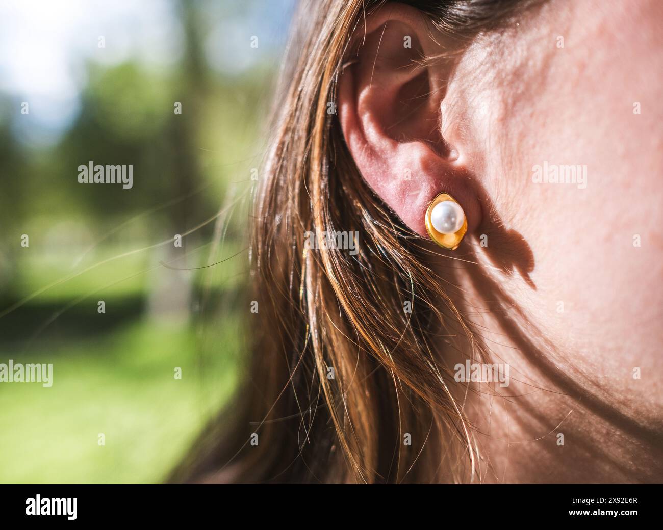 A young woman displays a gold and pearl earring worn on her right ear ...