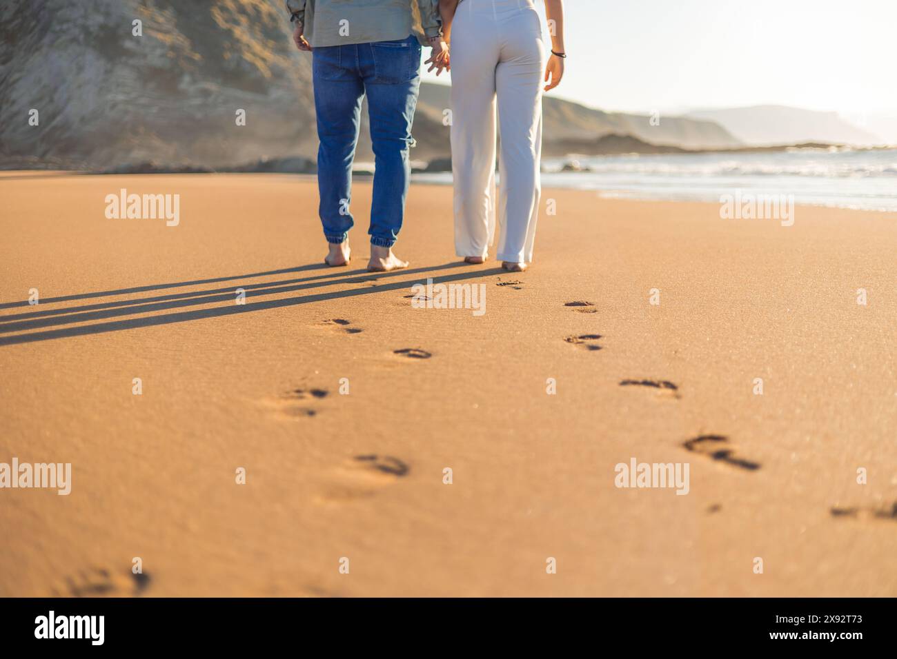anonymous couple walks hand in hand barefoot along the summer beach ...