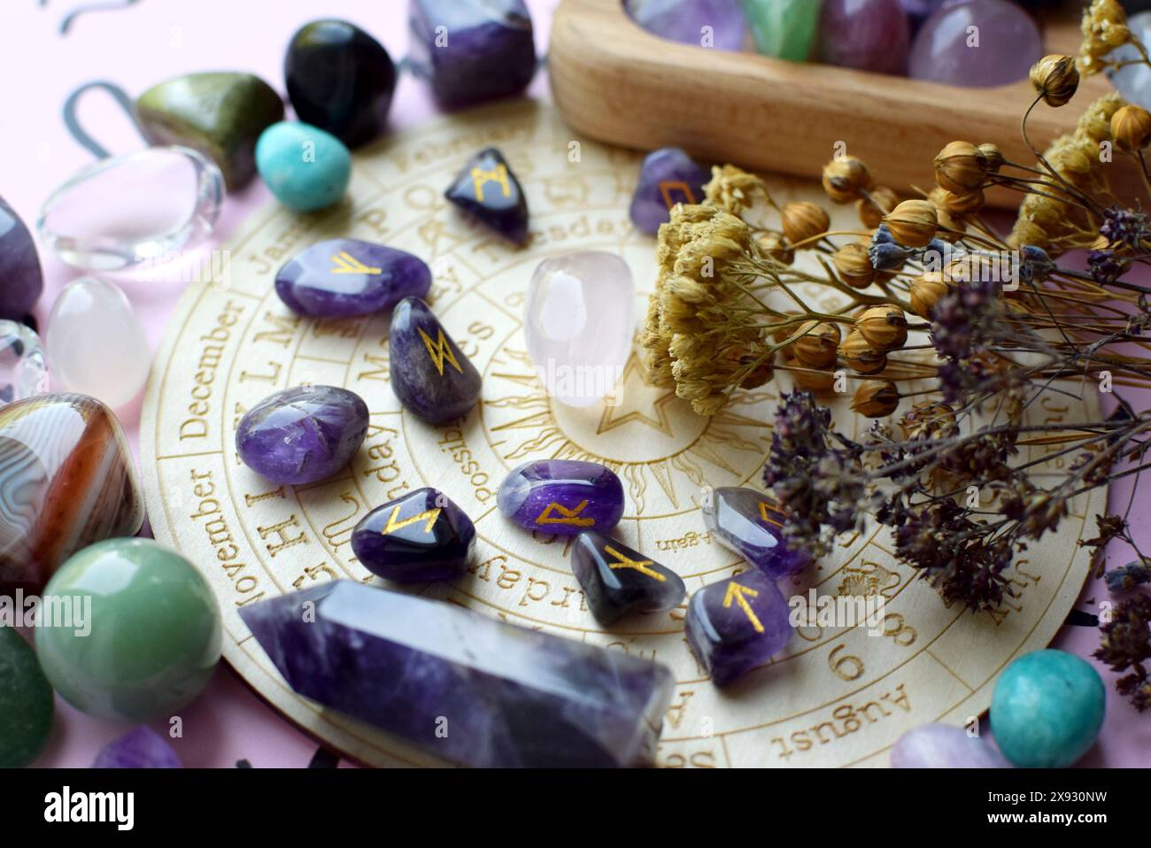 Scandinavian runes made of amethyst and dry herbs on a pink background ...