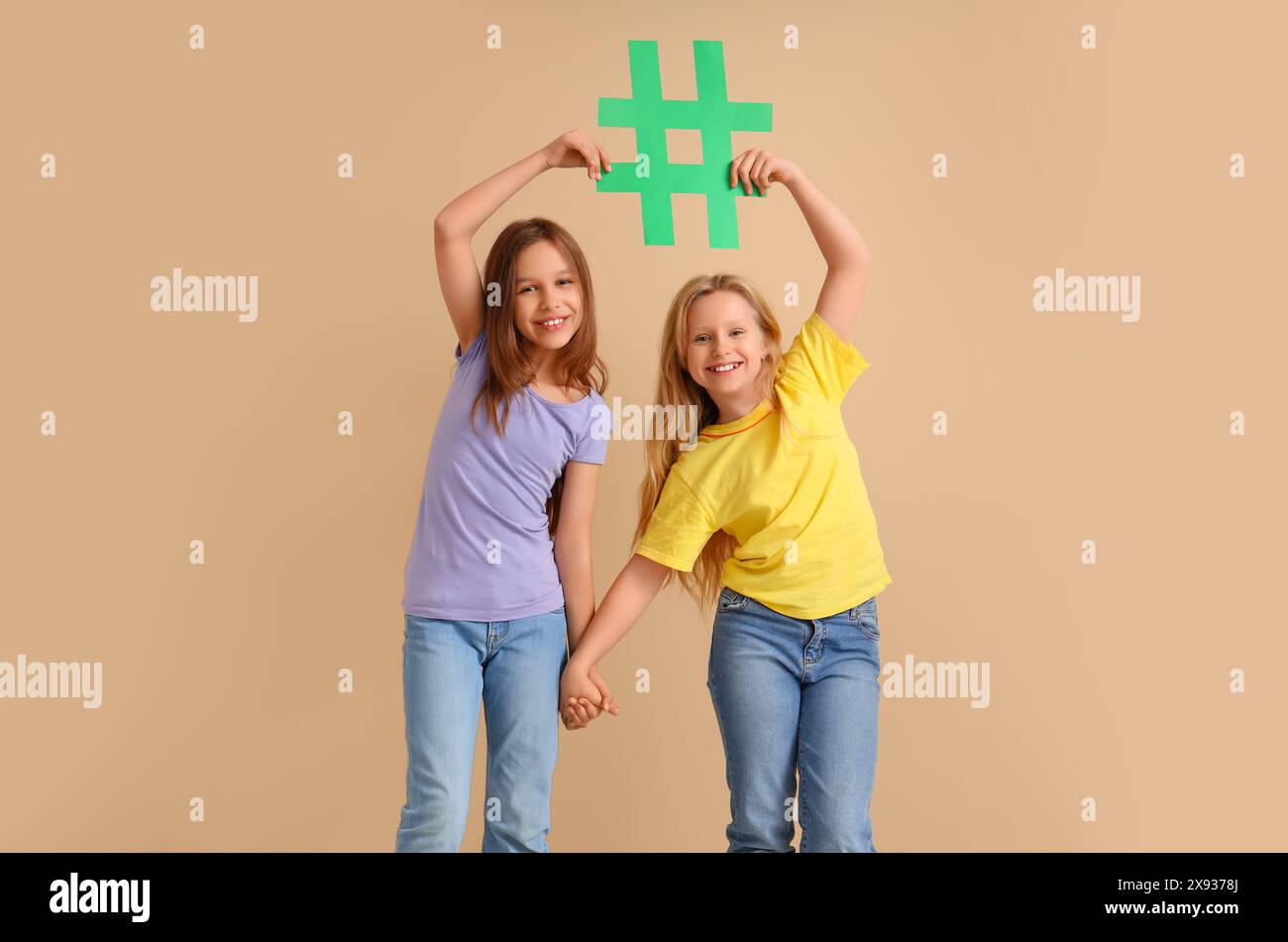 Cute girls with hashtag holding hands on beige background Stock Photo ...