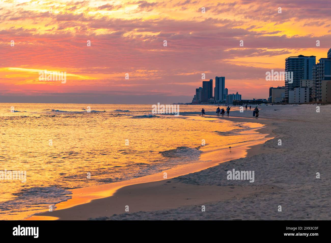 People walking along the shoreline of the beach at sunset on the Gulf ...