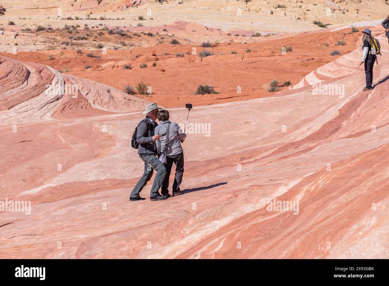 Couple use selfy stick for picture on a layered sandstone rock formation in the Fire Wave area ...