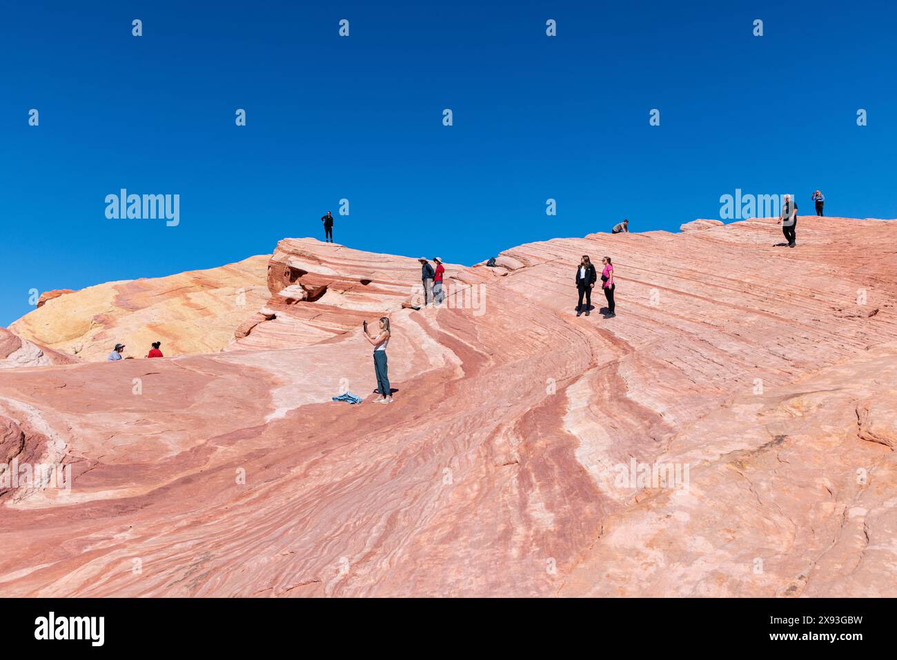 Hikers on layered sandstone rock formations in the Fire Wave area of Valley of Fire State Park ...