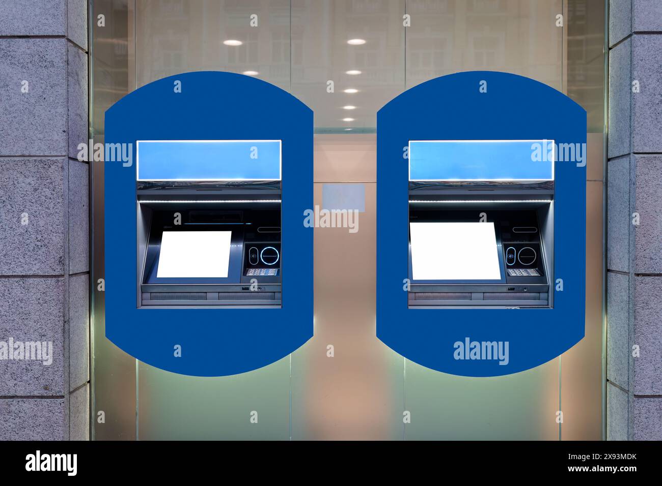 Two blue ATM machines with empty white screens on a wall outside a ...