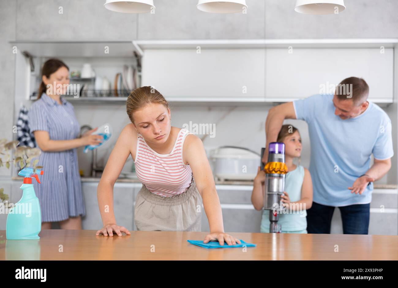 Teenage daughter dusting the table while parents and youngest daughter ...