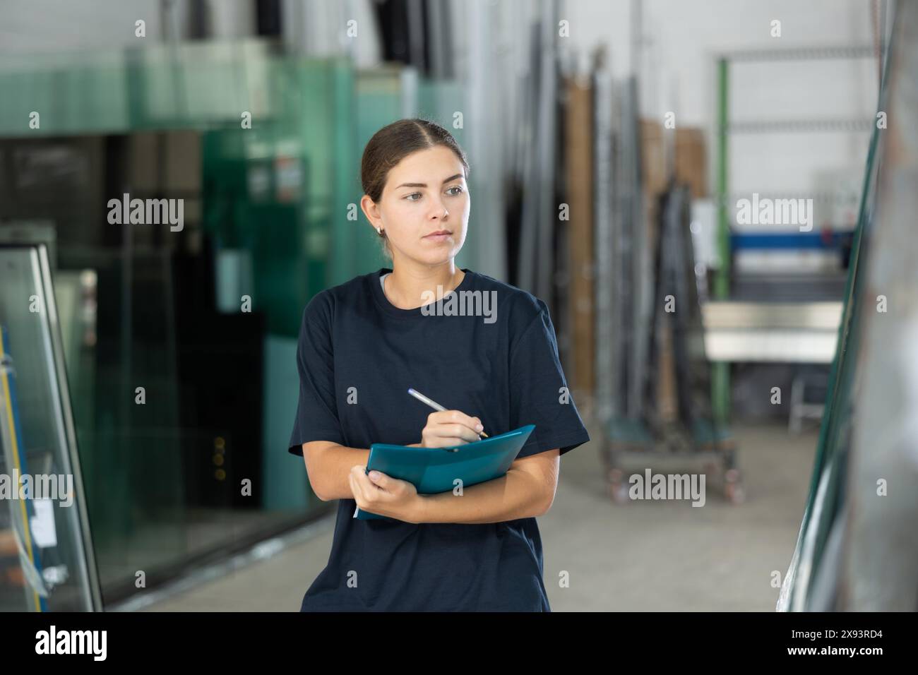 Female worker inspecting glass panels and writing on clipboard in ...