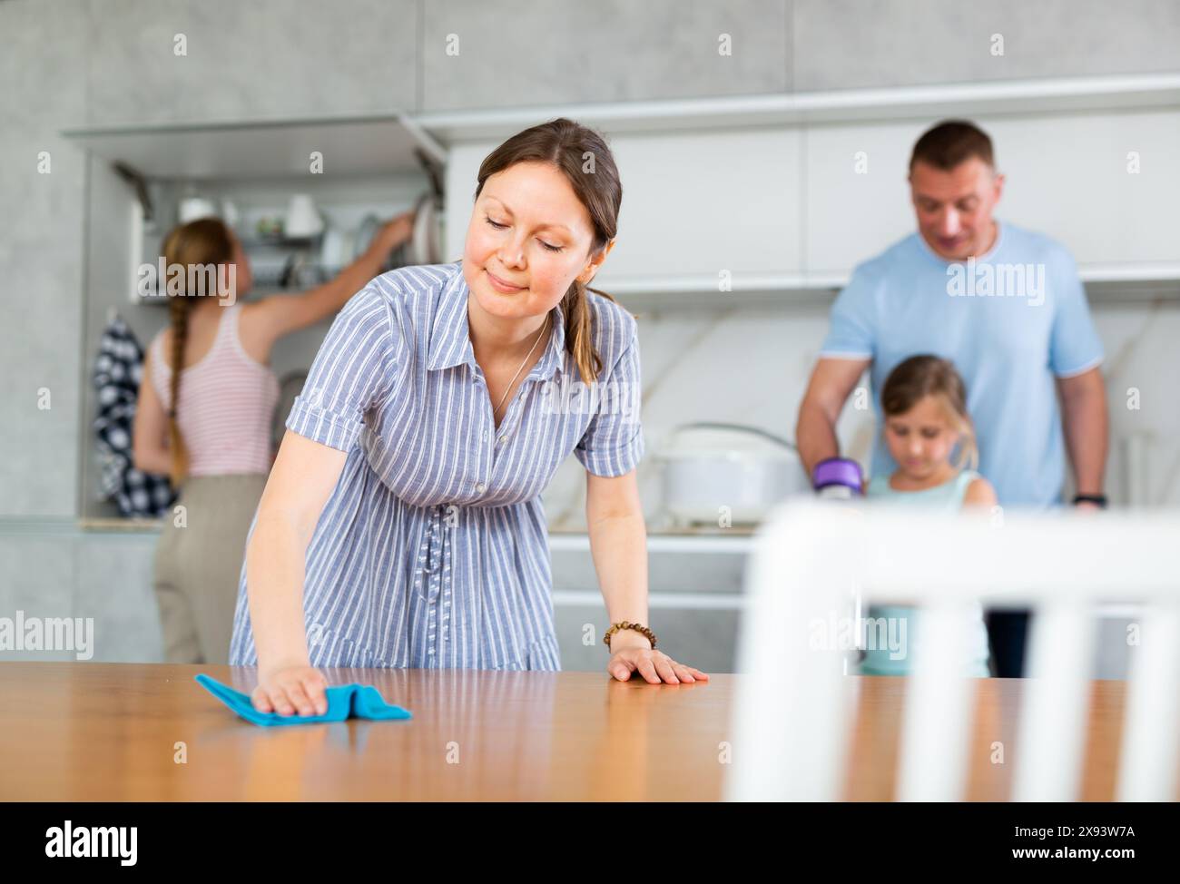 Woman rubbing table in kitchen while cleaning house with family Stock ...