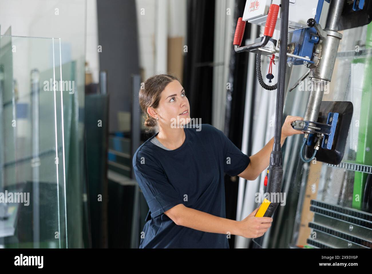 Female operator maneuvering glass sheets with vacuum lifter in workshop ...