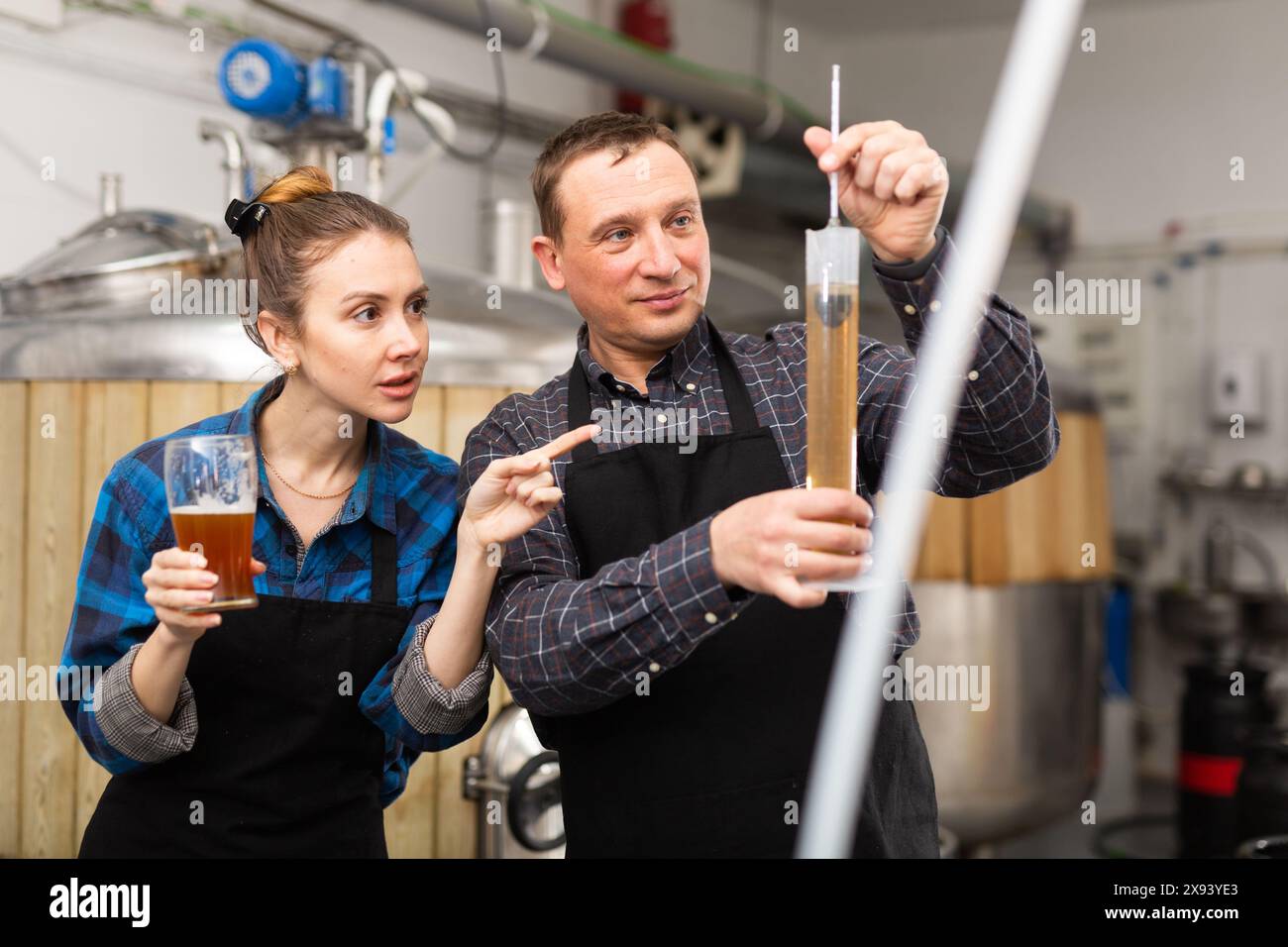 Experienced brewer with female assistant measuring beer gravity with ...