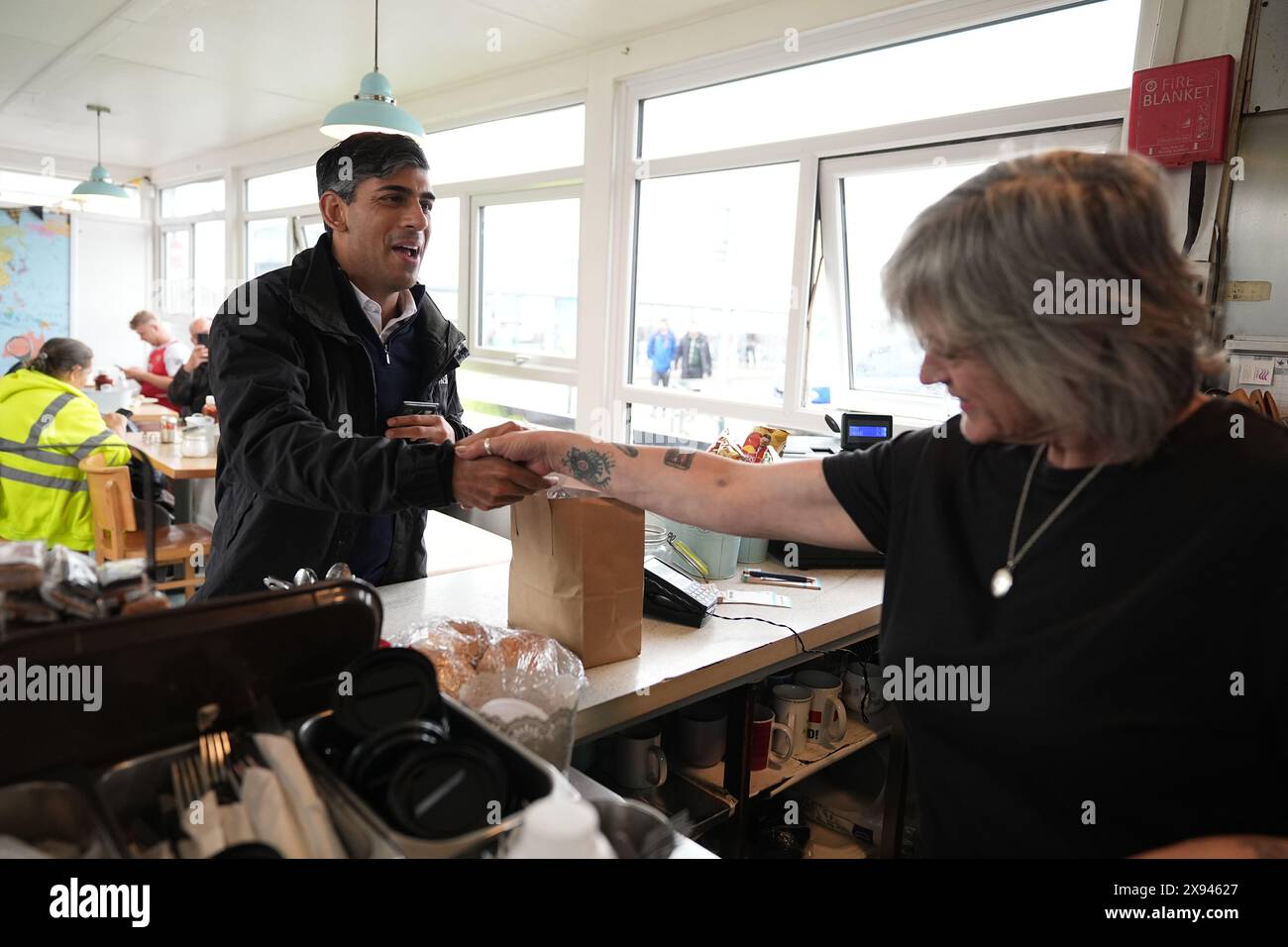 Prime Minister Rishi Sunak shakes hands with a cafe worker as he picks ...