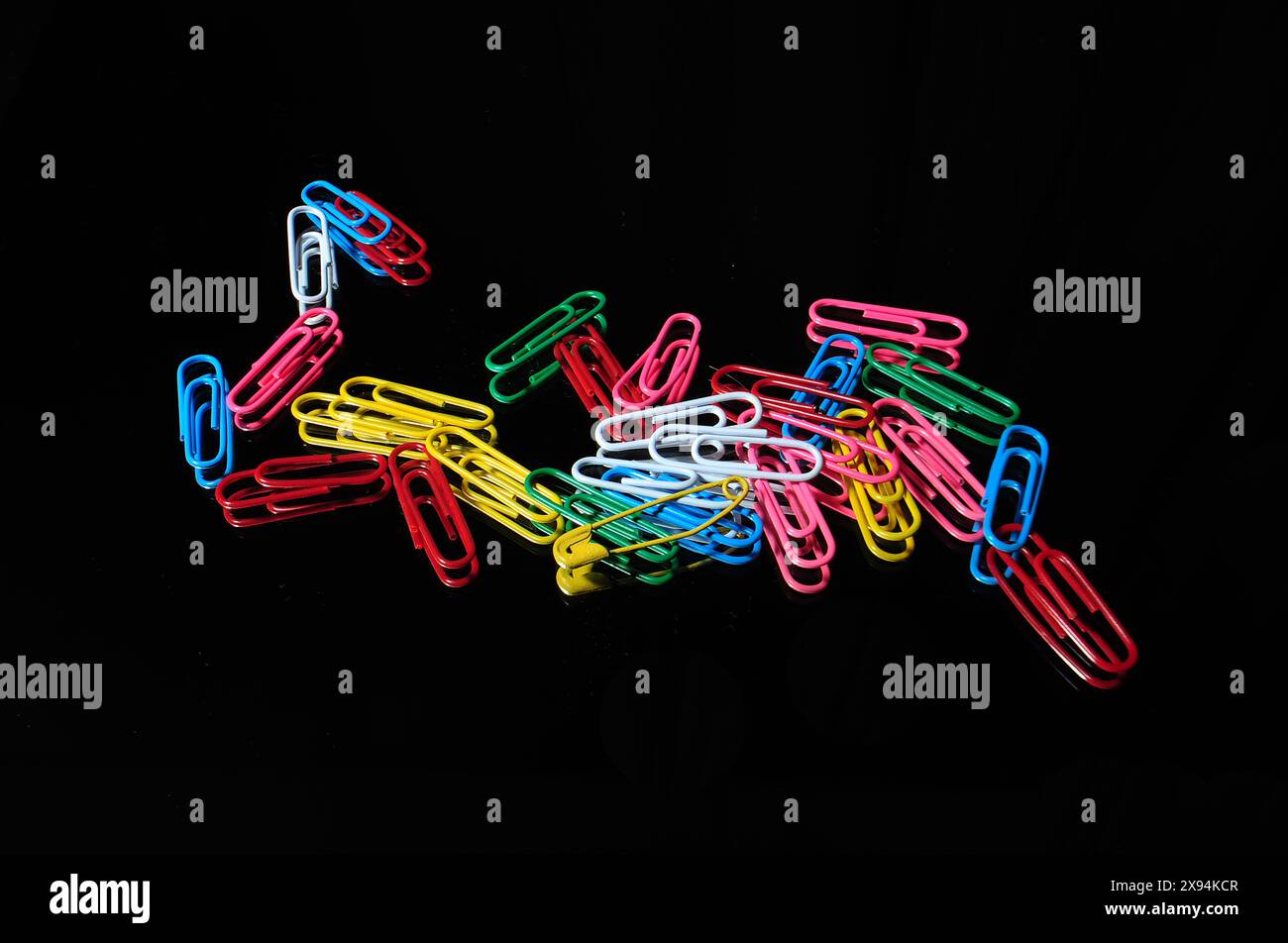 One single yellow safety pin along with multiple colorful paper clips ...