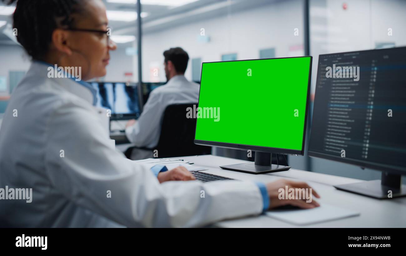 Black Female Medical Doctor is Working on Computer with Green Screen Mock Up Display in a ...