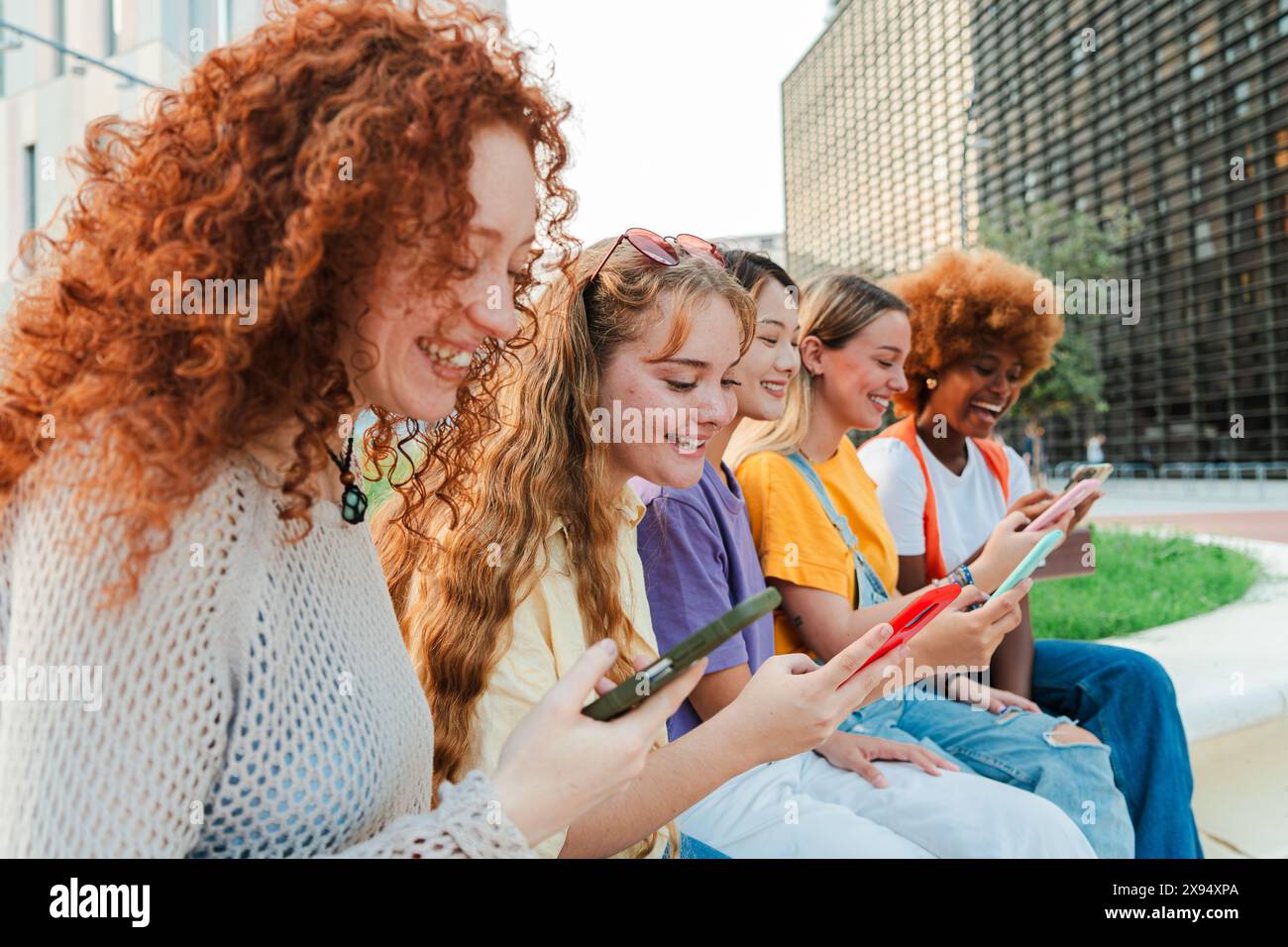A lively group of diverse teenagers sits together outdoors, fully ...
