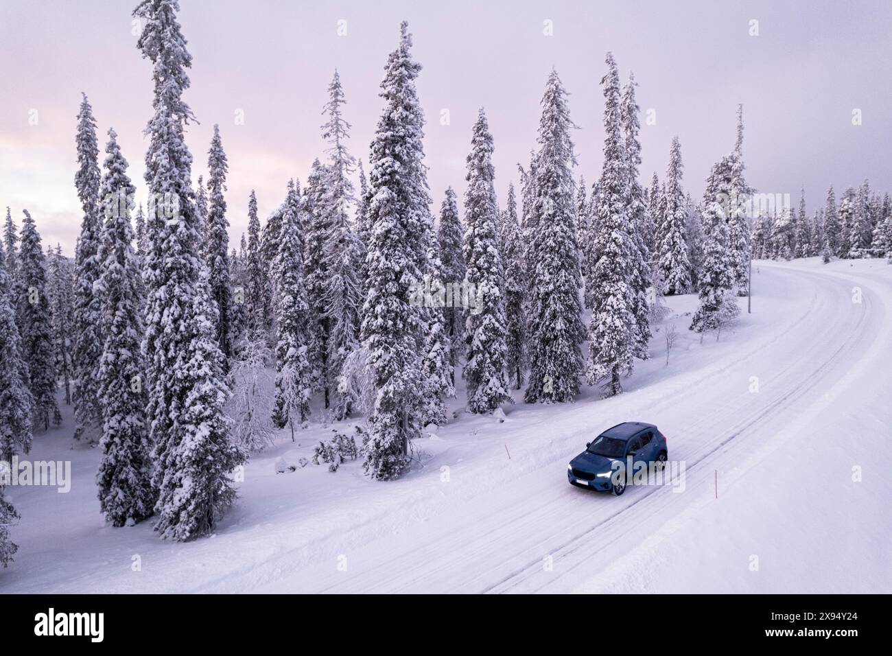 Aerial shot of a car driving across snow-capped forest in the Arctic ...