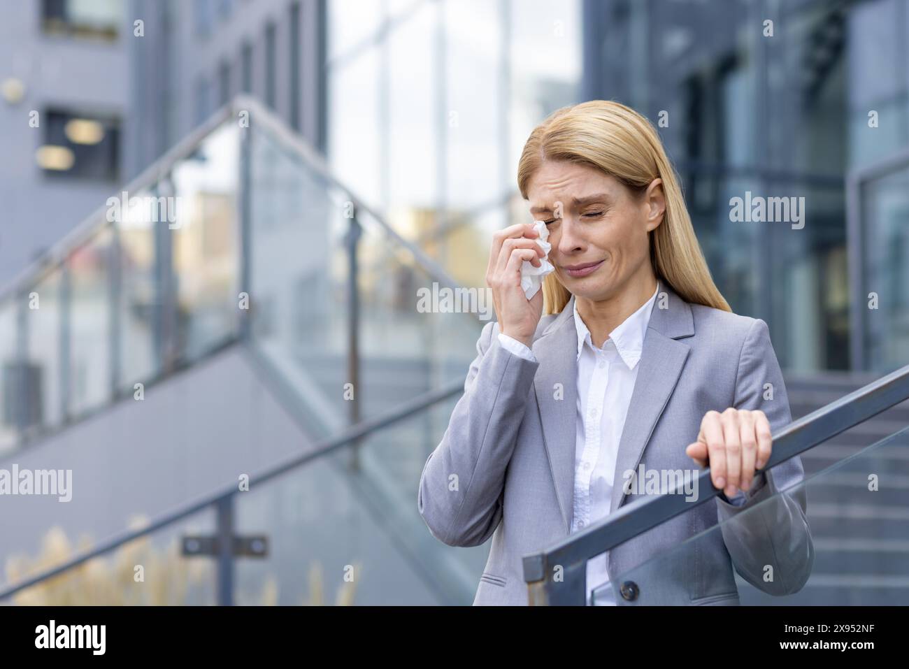 Businesswoman in a suit crying on stairs outside an office building ...