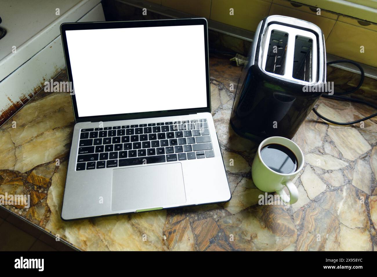 A laptop is open on a table with a toaster and a cup of coffee. the ...