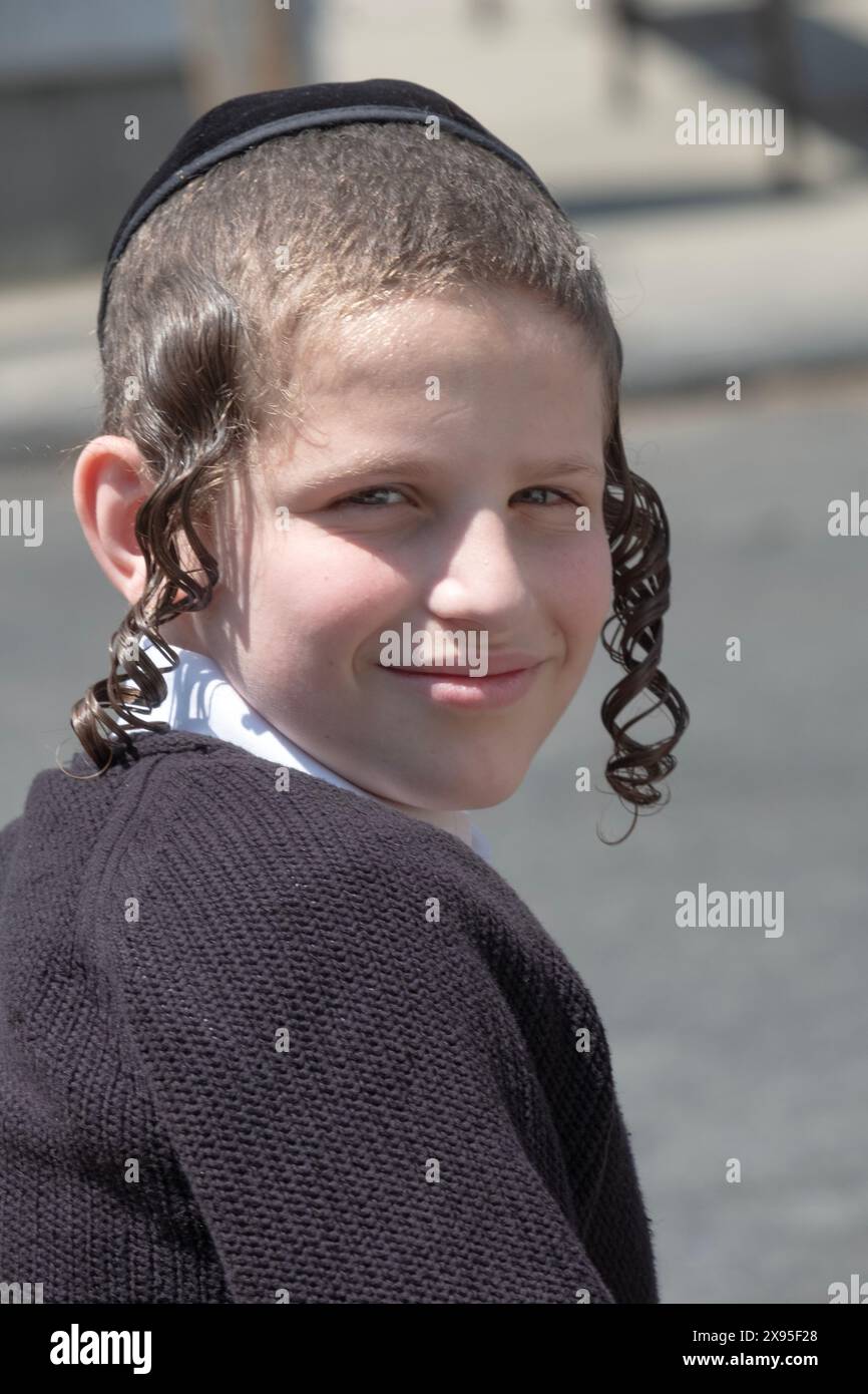 A posed portrait of a Hasidic Jewish boy with long curly peyus. At a ...