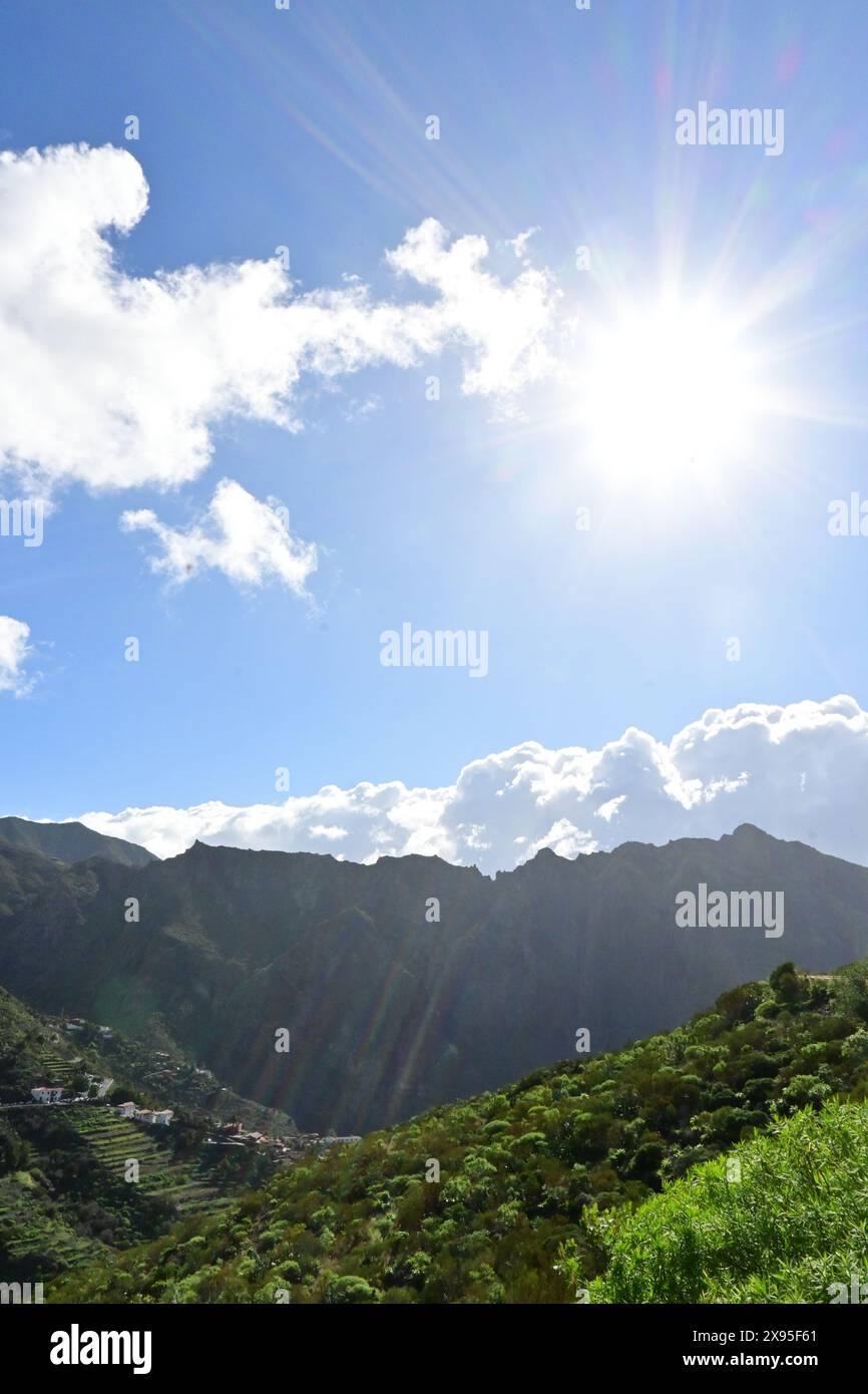 Sun shining brightly over green hills and dramatic mountain peaks, with ...