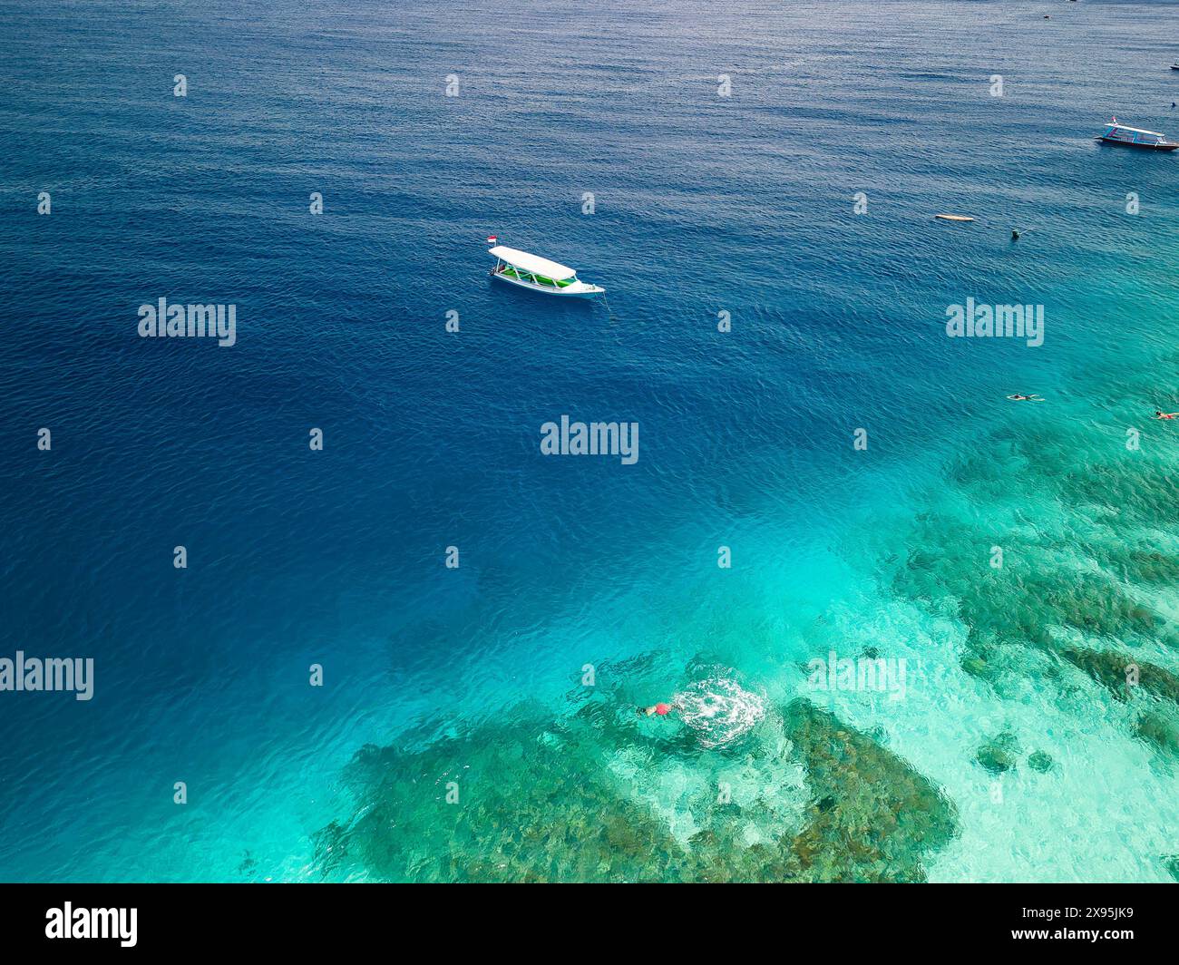 Snorkelers and tour boats over a shallow tropical coral reef (Gili ...