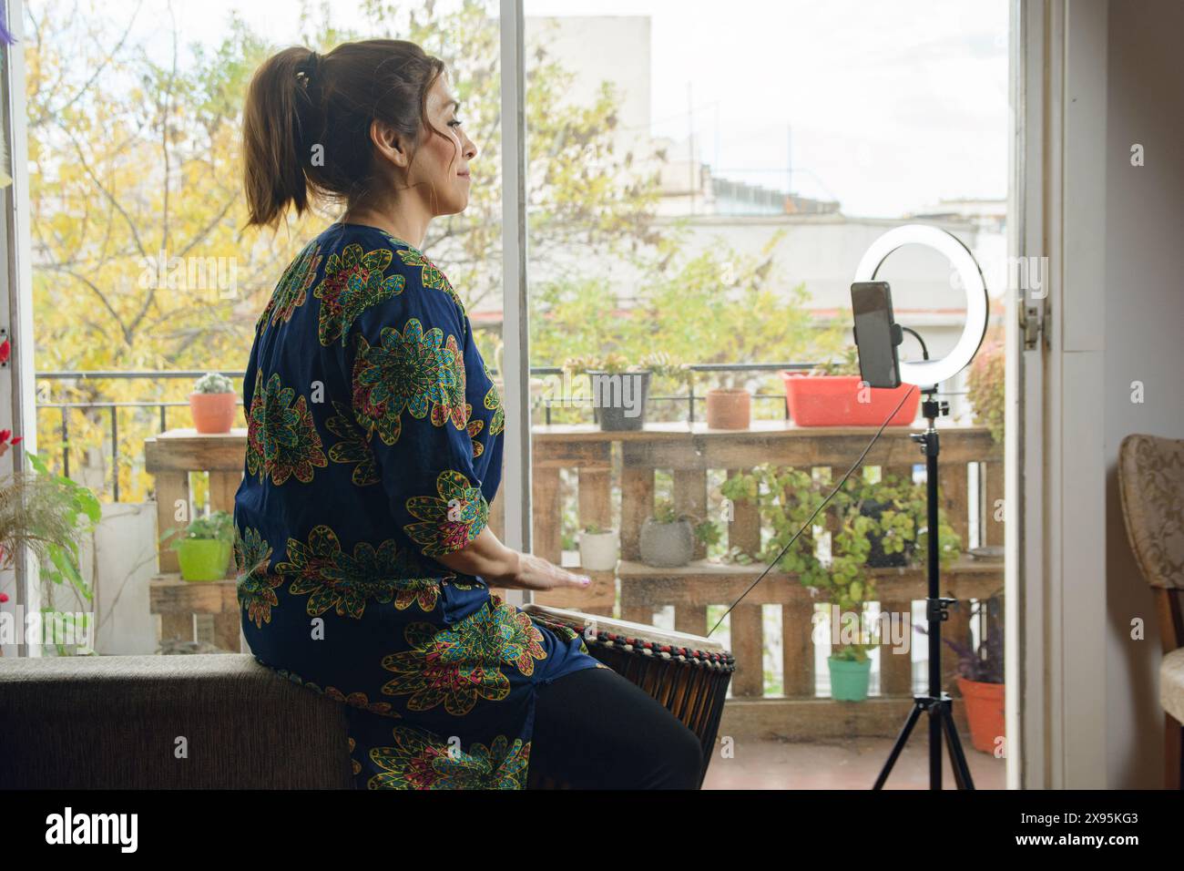 Rear view of Woman at home sitting on the sofa playing the Djembe drum ...