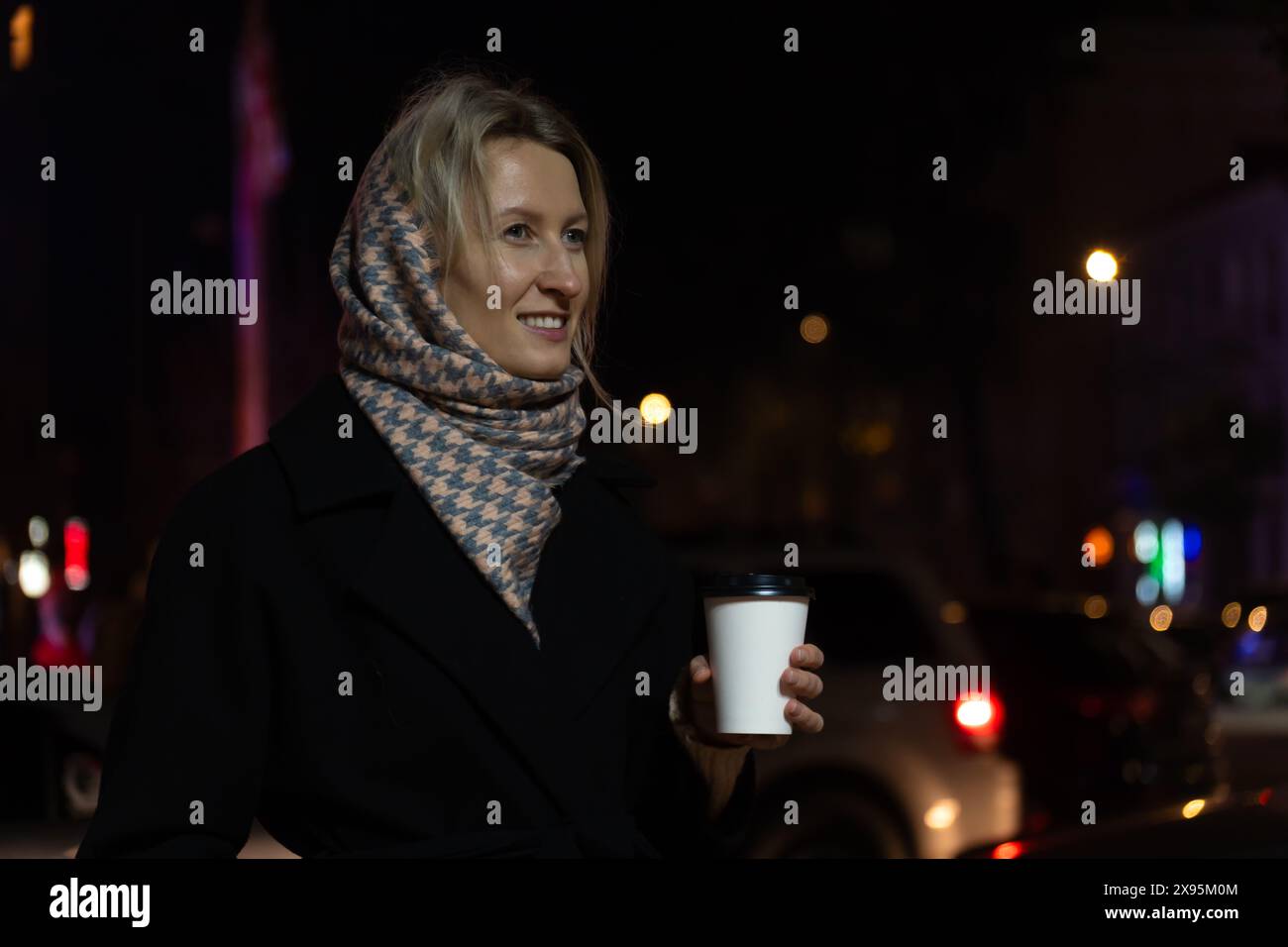 Young beautiful woman in a stole and a black coat drinks takeaway ...