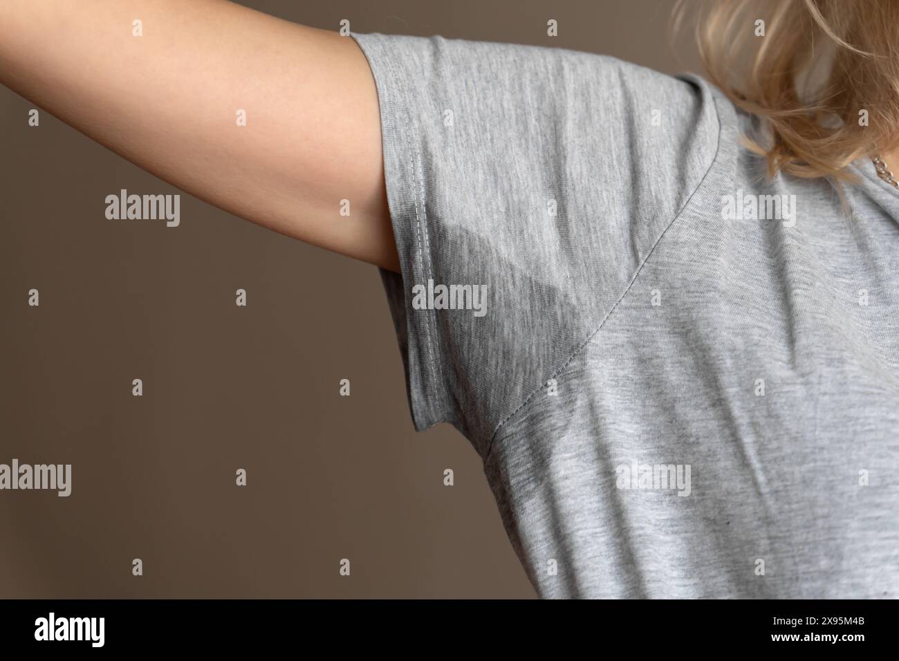 Close-up of a young woman shows a wet armpit on a gray T-shirt. Concept ...
