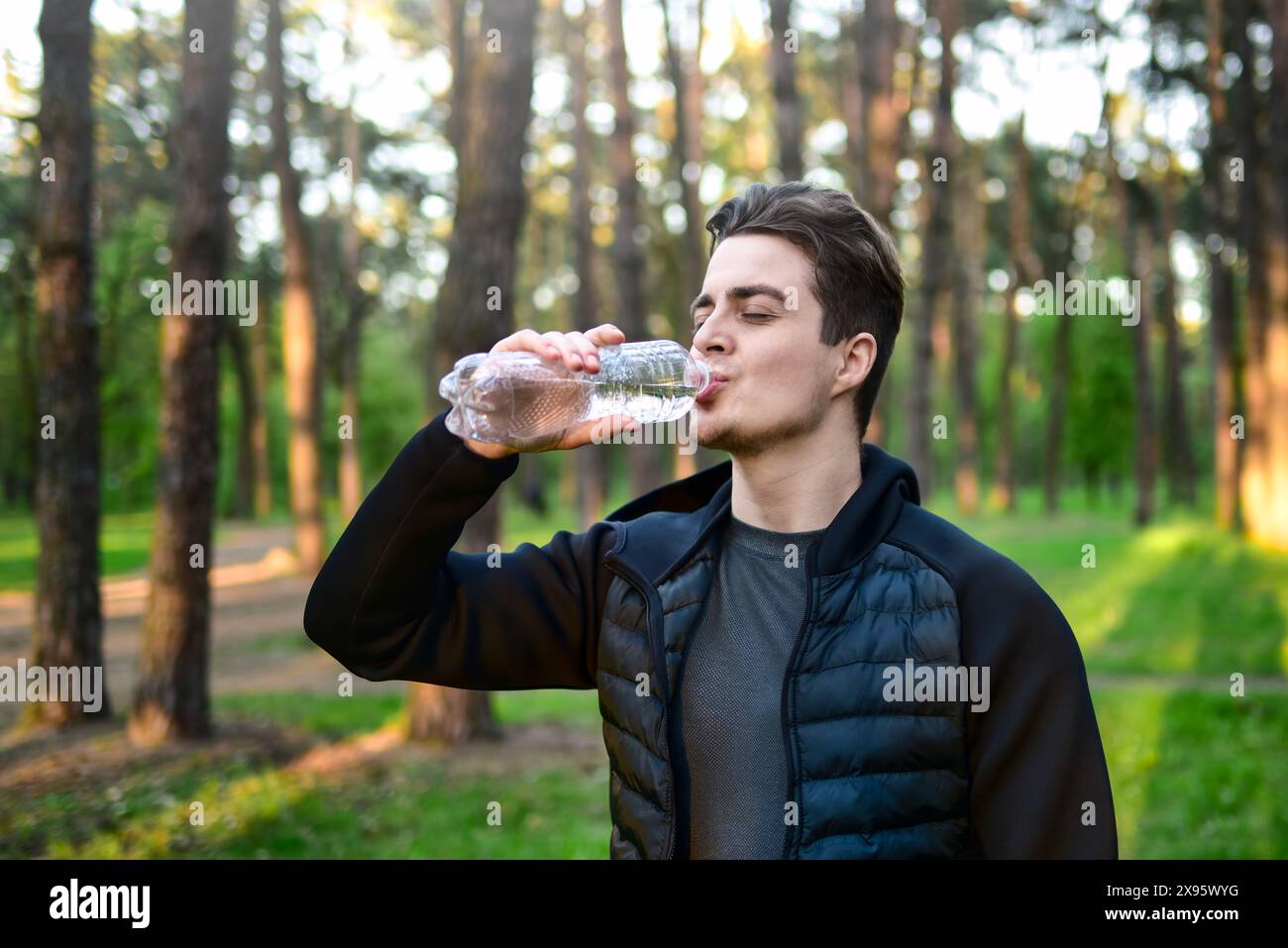 A handsome young man in a sports jacket drinking water from a bottle in ...
