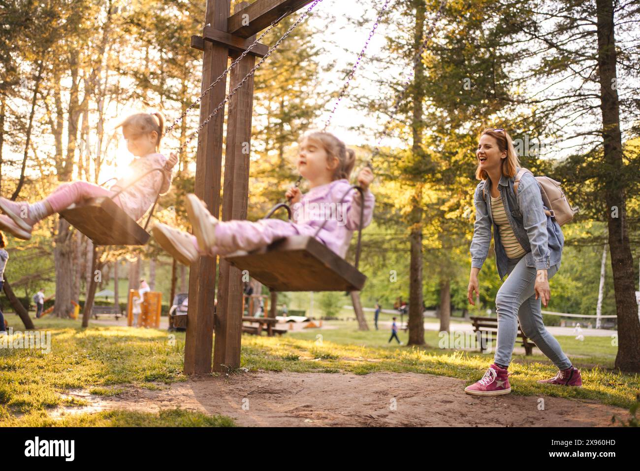 Mother is rocking her twin daughters on a swing in the park Stock Photo ...