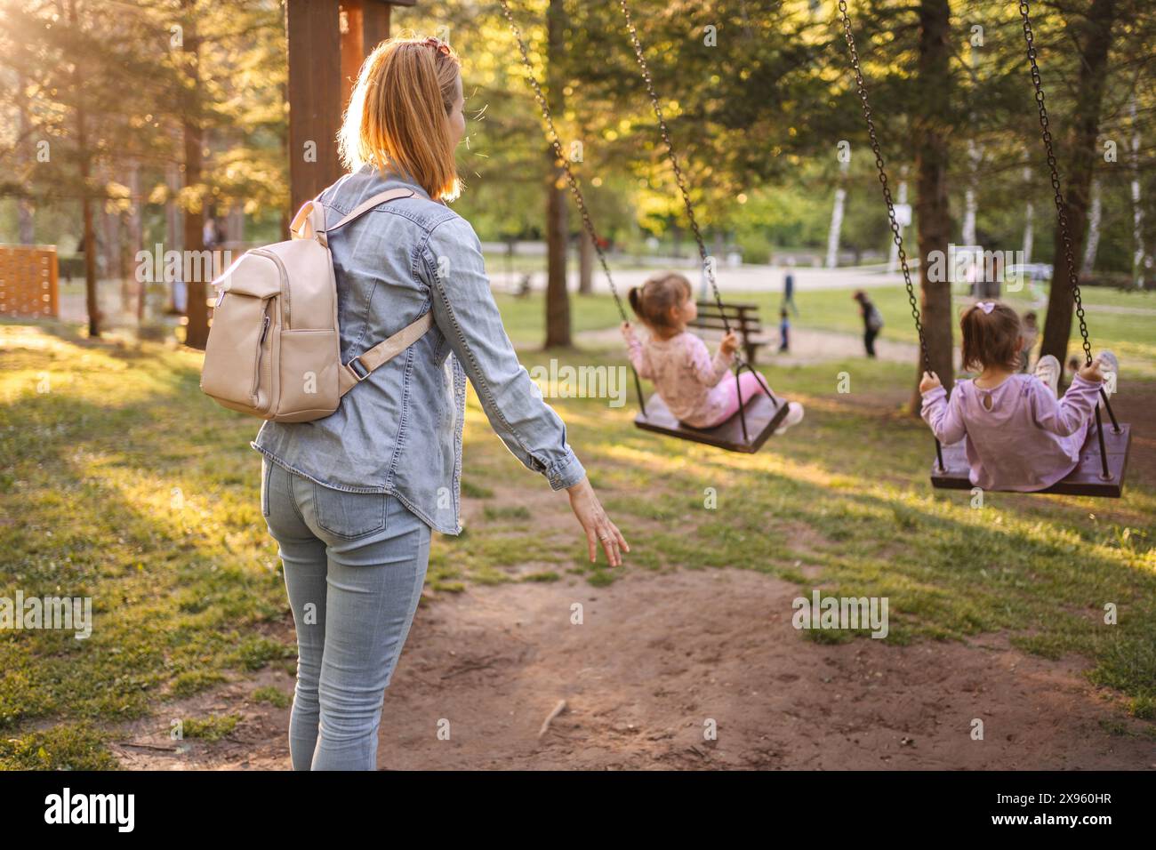 Mother is rocking her twin daughters on a swing in the park Stock Photo ...