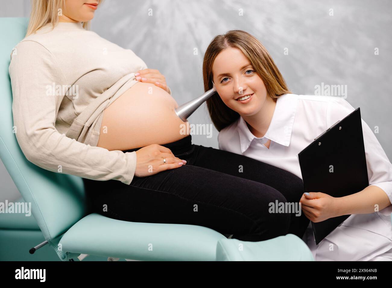 A gynecologist leans a stethoscope to a pregnant woman's belly and ...