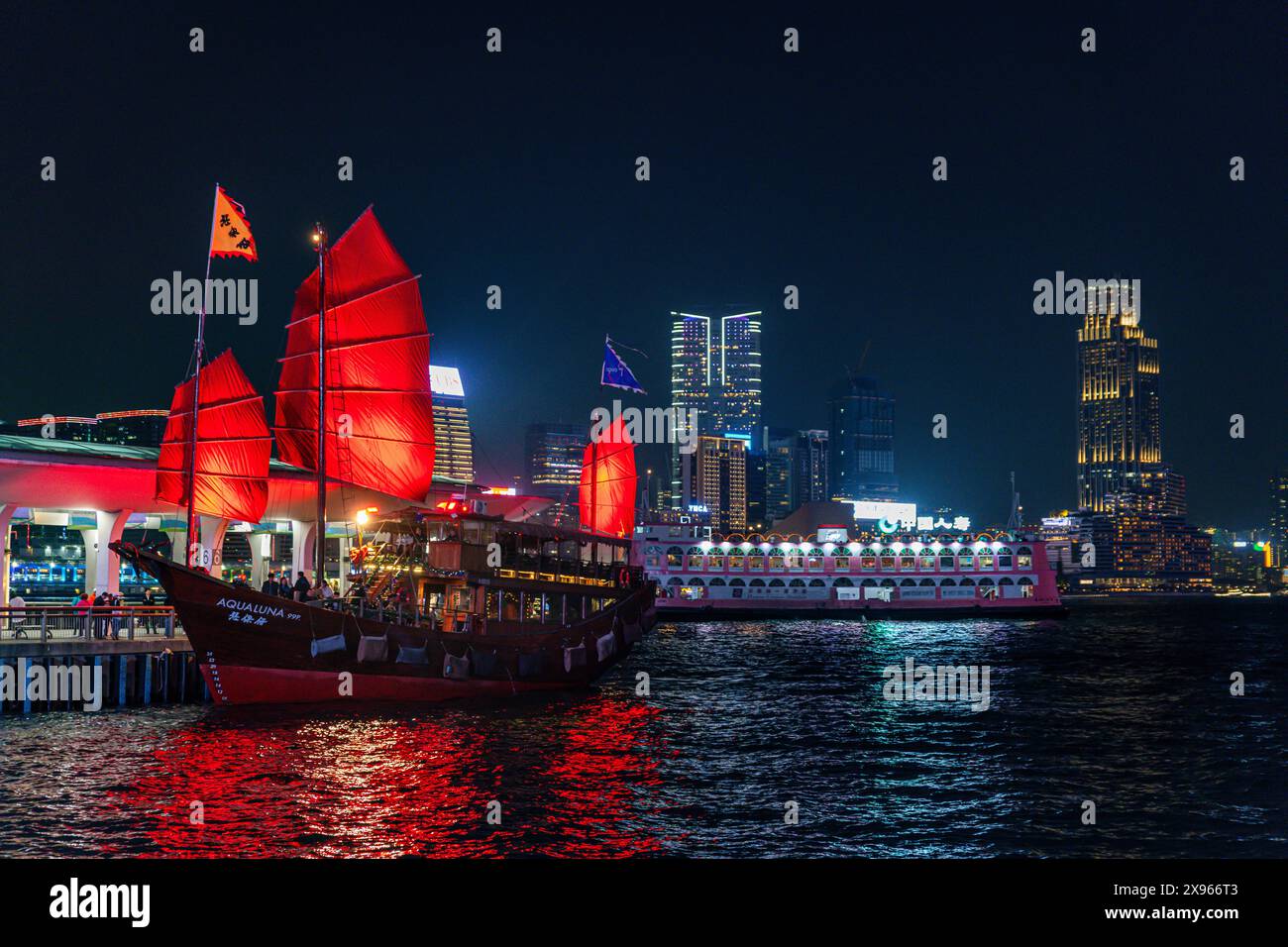 Traditional sailing boat with red sails at night, with high rise buildings behind in Central ...