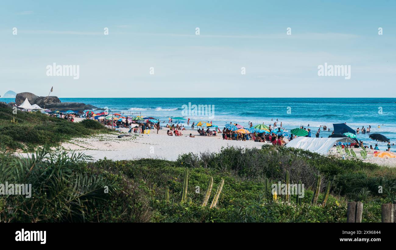 Crowds of beachgoers relax under colorful umbrellas on a sandy ...