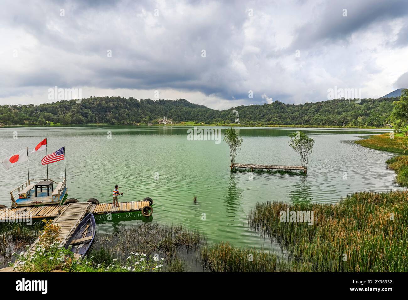 Boy fishing on dock by changing colour Lake Linow, a popular volcanic ...