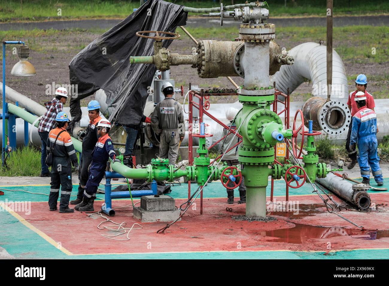 Workers in hard hats by steam pipes and valves at a volcanic facility ...