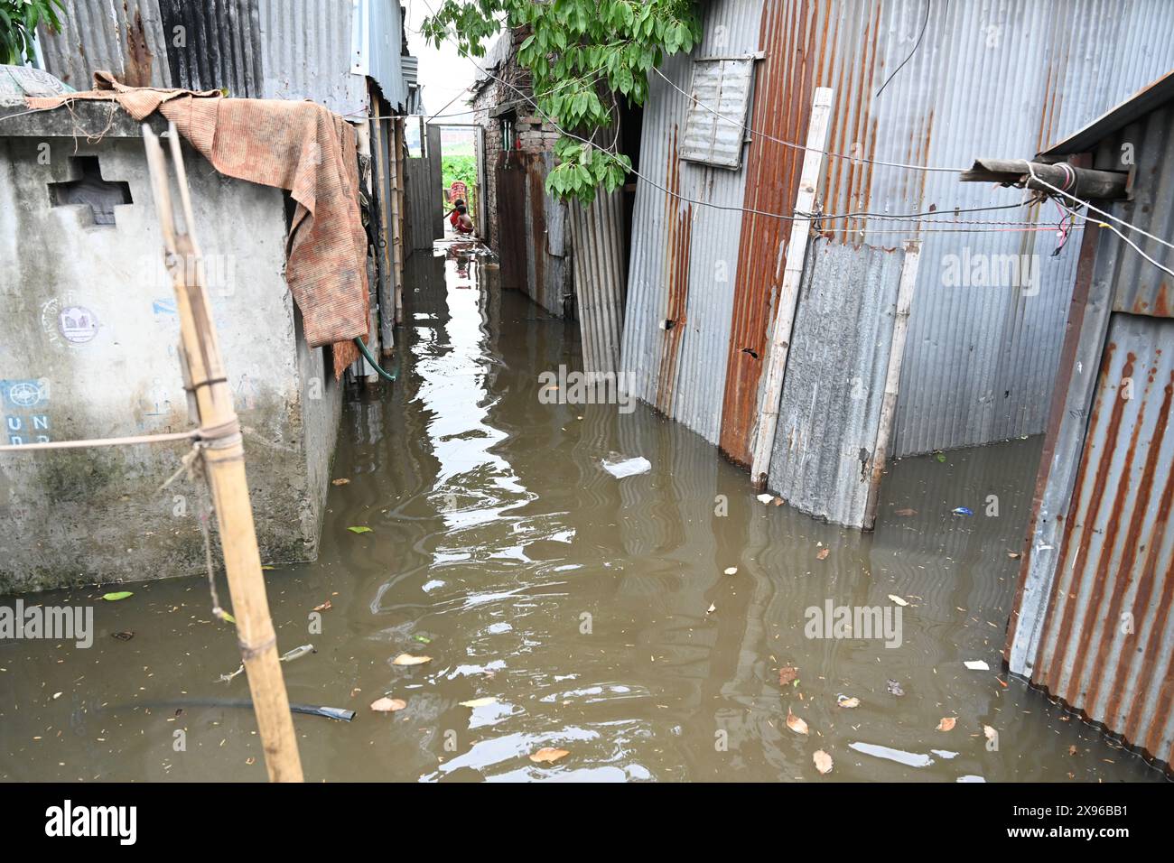 Slum people wades through a flooded courtyard following heavy rains ...