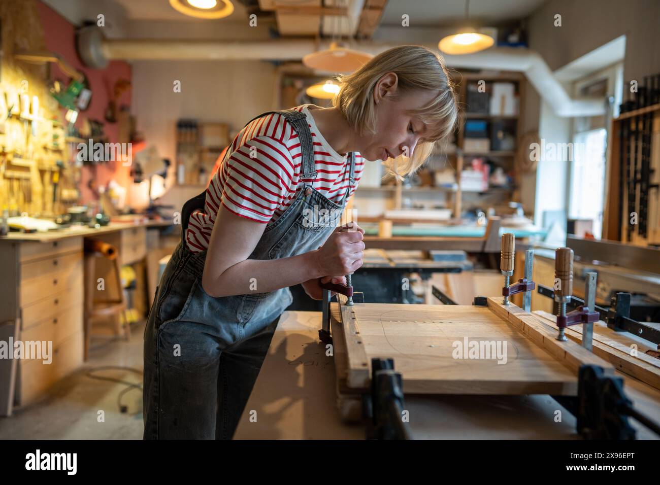 Concentrated female carpenter working on gluing wooden planks together ...