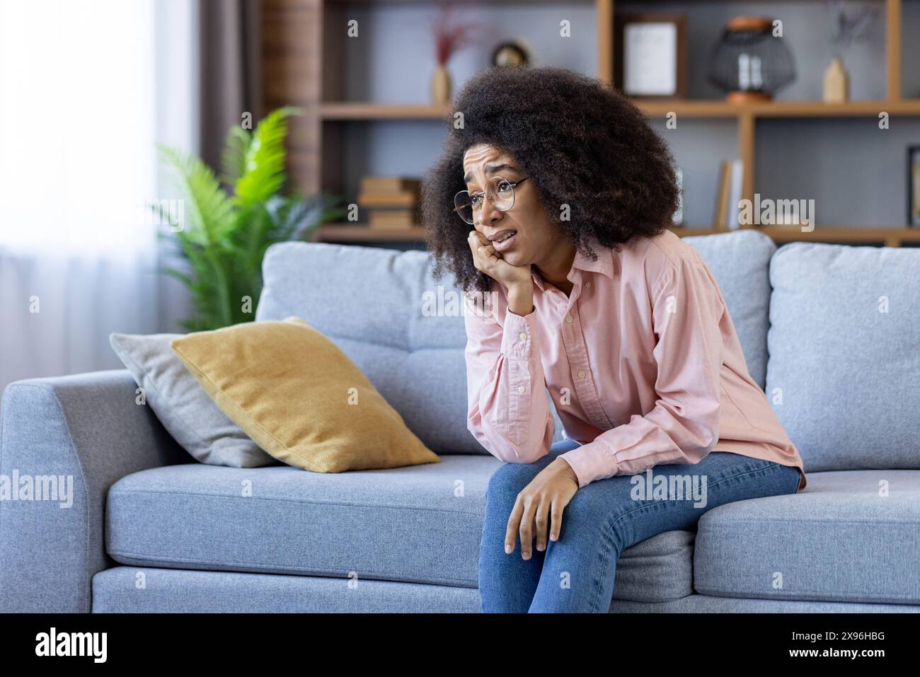 A worried woman sitting on a couch, feeling stressed and anxious in a ...