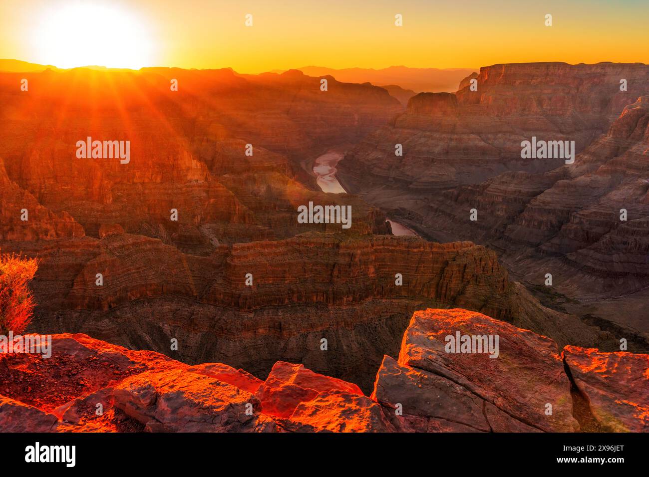 Sun is visible at the horizon over the Grand Canyon, casting a warm ...