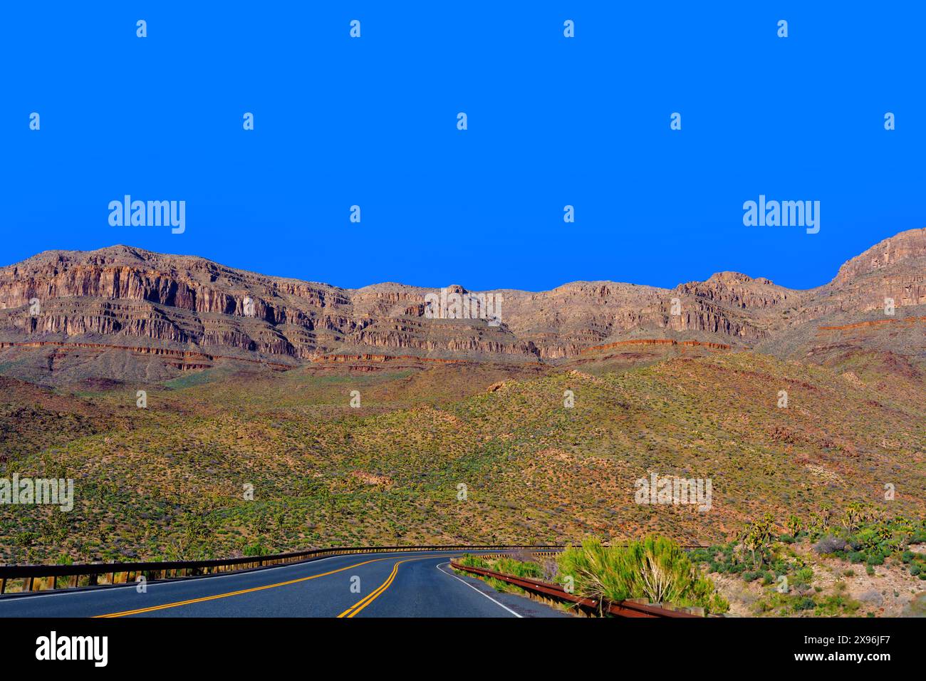 Asphalt road with bright yellow dividing lines leads along the majestic ...