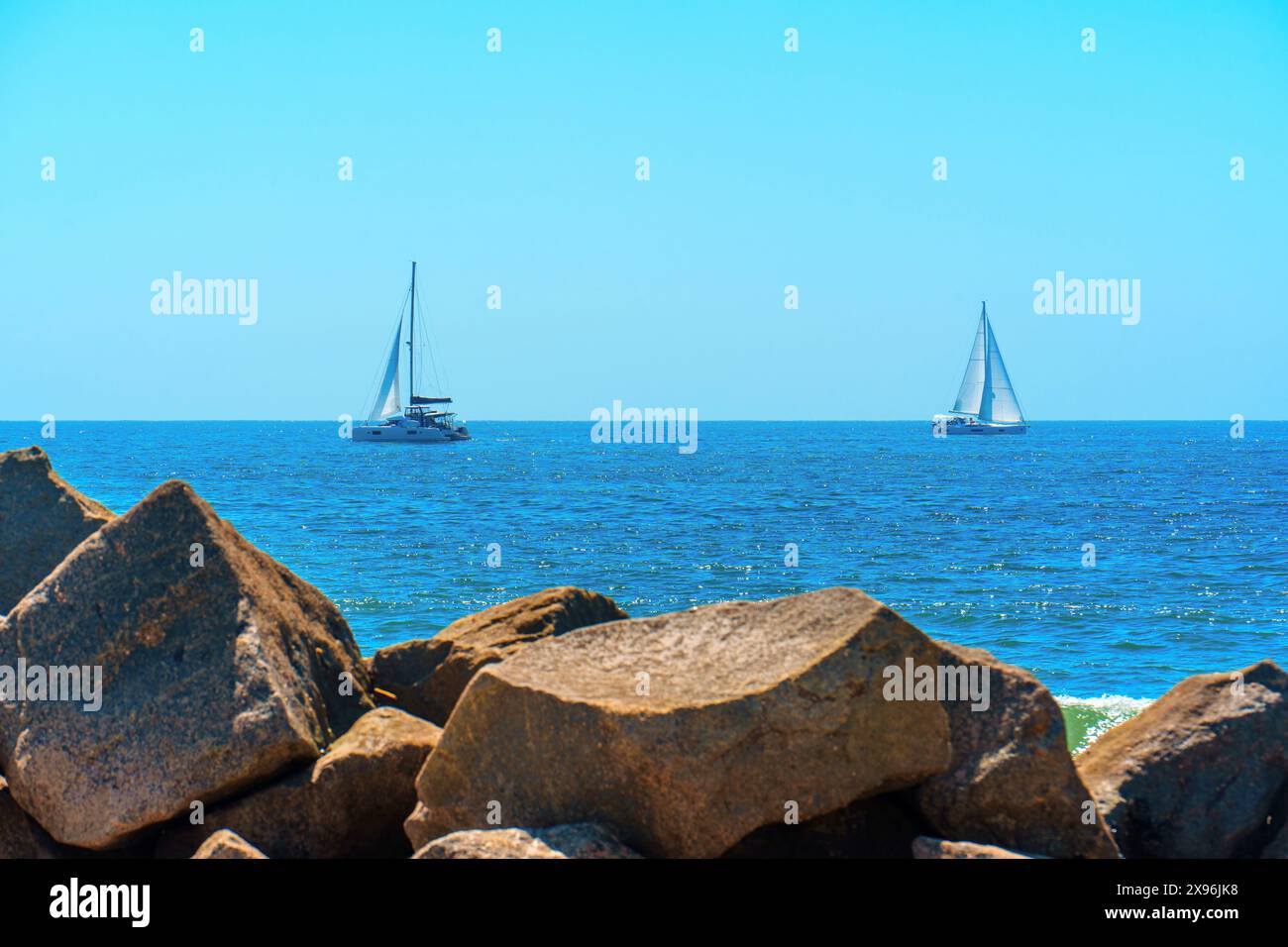 Two sailboats peacefully sail in the ocean seen through the rugged ...