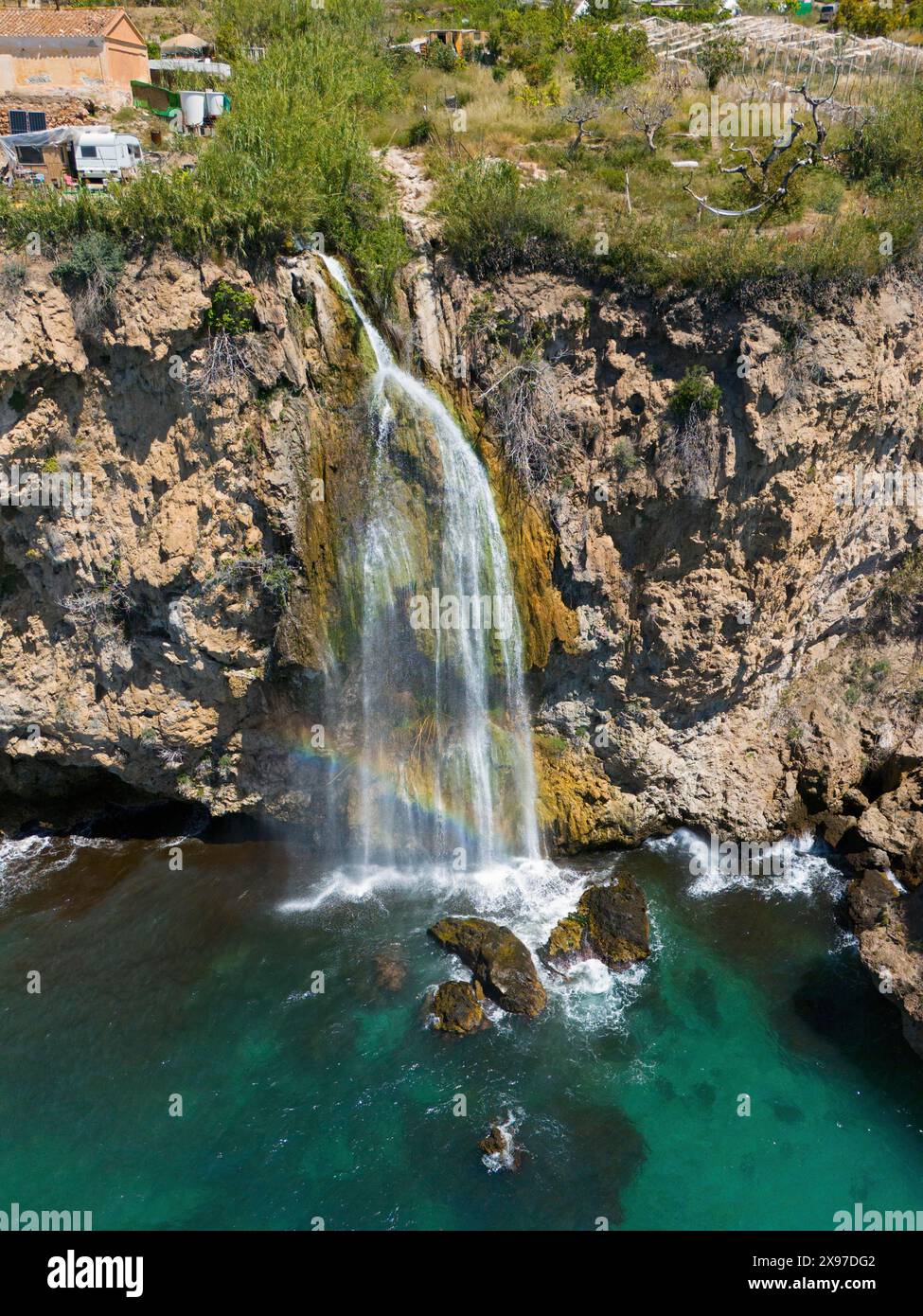 A waterfall cascades from a cliff into turquoise-coloured water in a ...